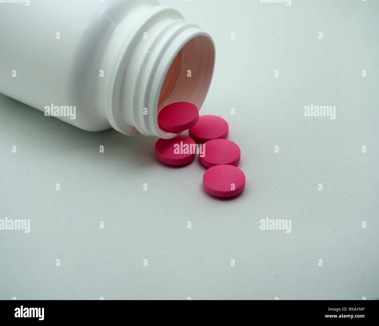 Red tablets are poured from a white plastic jar. Photo on white ...