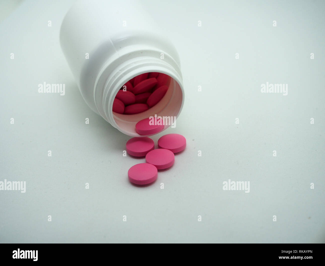 Red tablets are poured from a white plastic jar. Photo on white ...