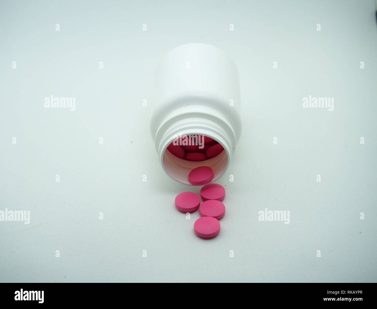 Red tablets are poured from a white plastic jar. Photo on white ...