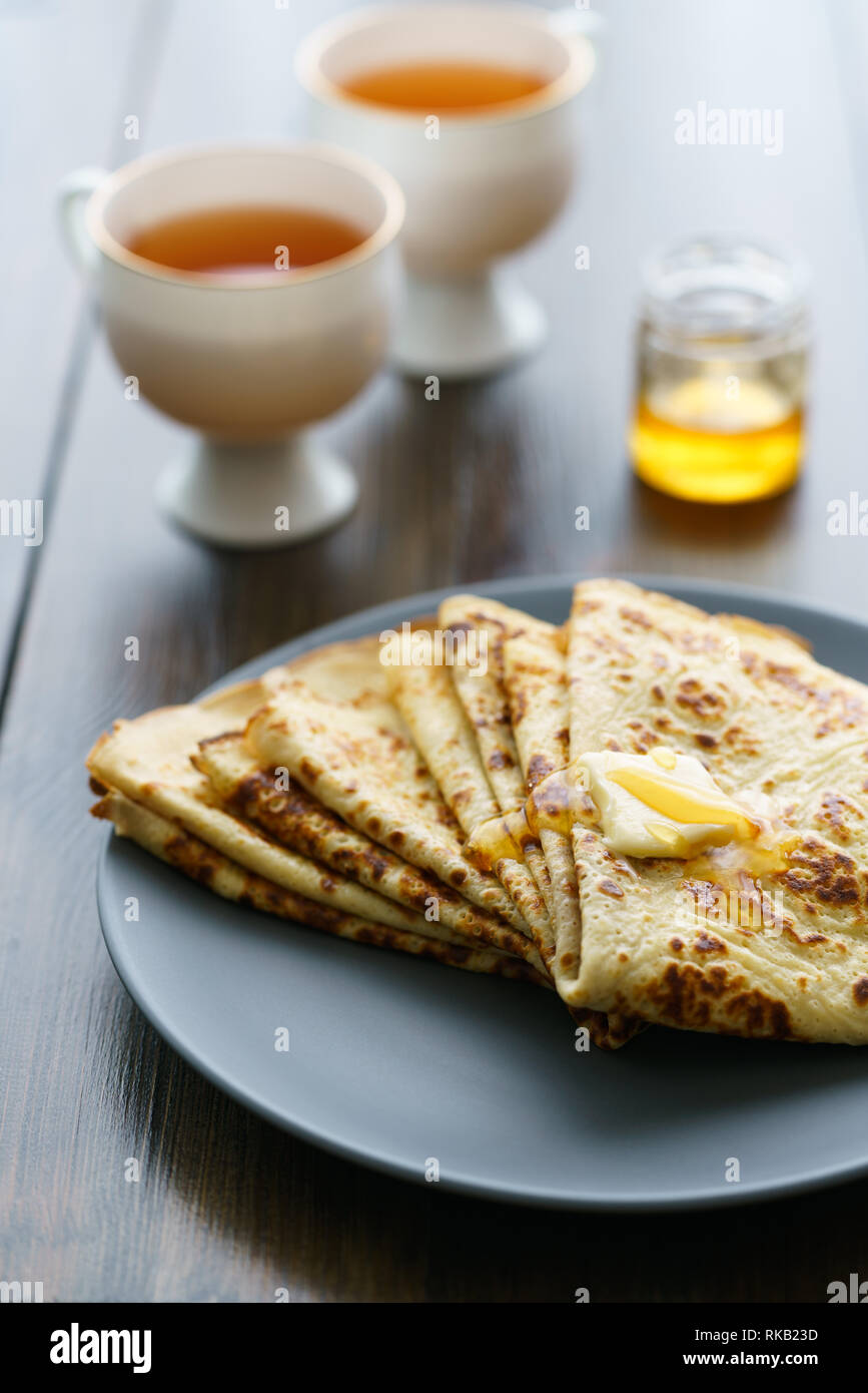 Crepes on a grey ceramic plate served with honey and 2 cups of tea ...