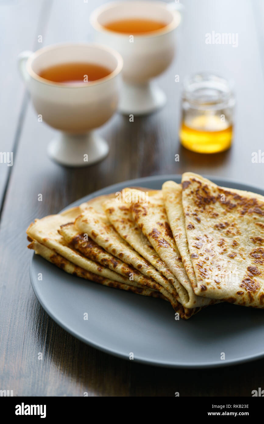 Crepes on a grey ceramic plate served with honey and 2 cups of tea ...