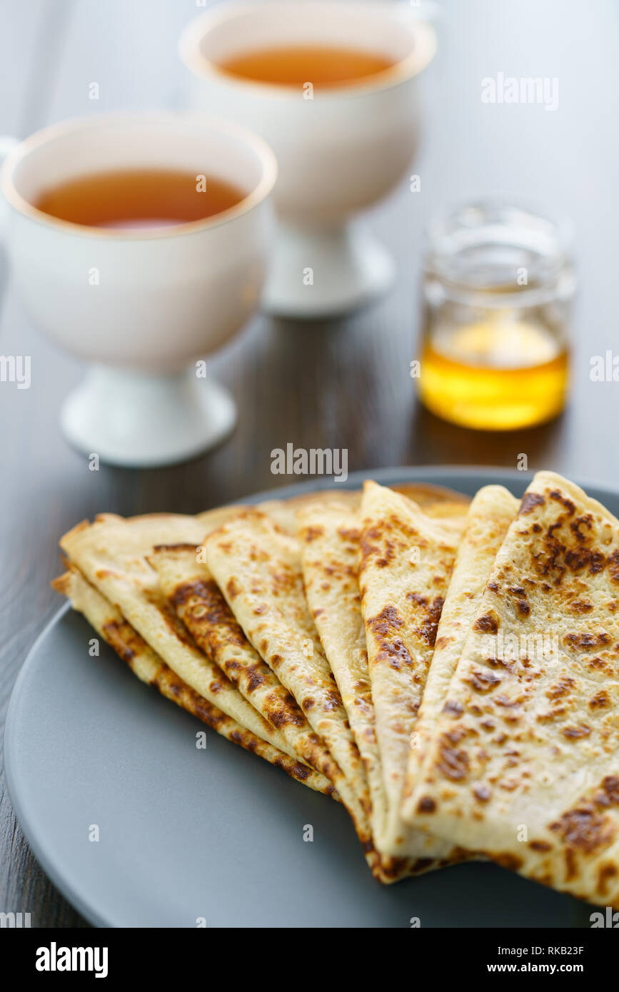 Crepes on a grey ceramic plate served with honey and 2 cups of tea ...