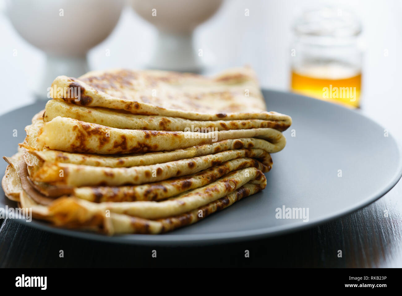 Crepes on a grey ceramic plate served with honey and 2 cups of tea ...