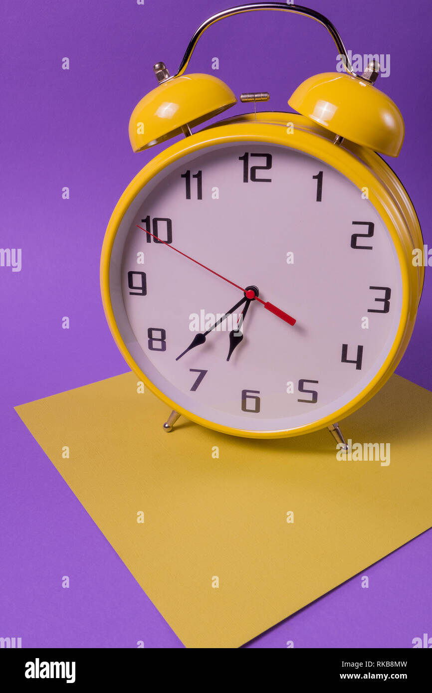 Yellow alarm clock with twenty two minutes to seven o'clock on purple ...