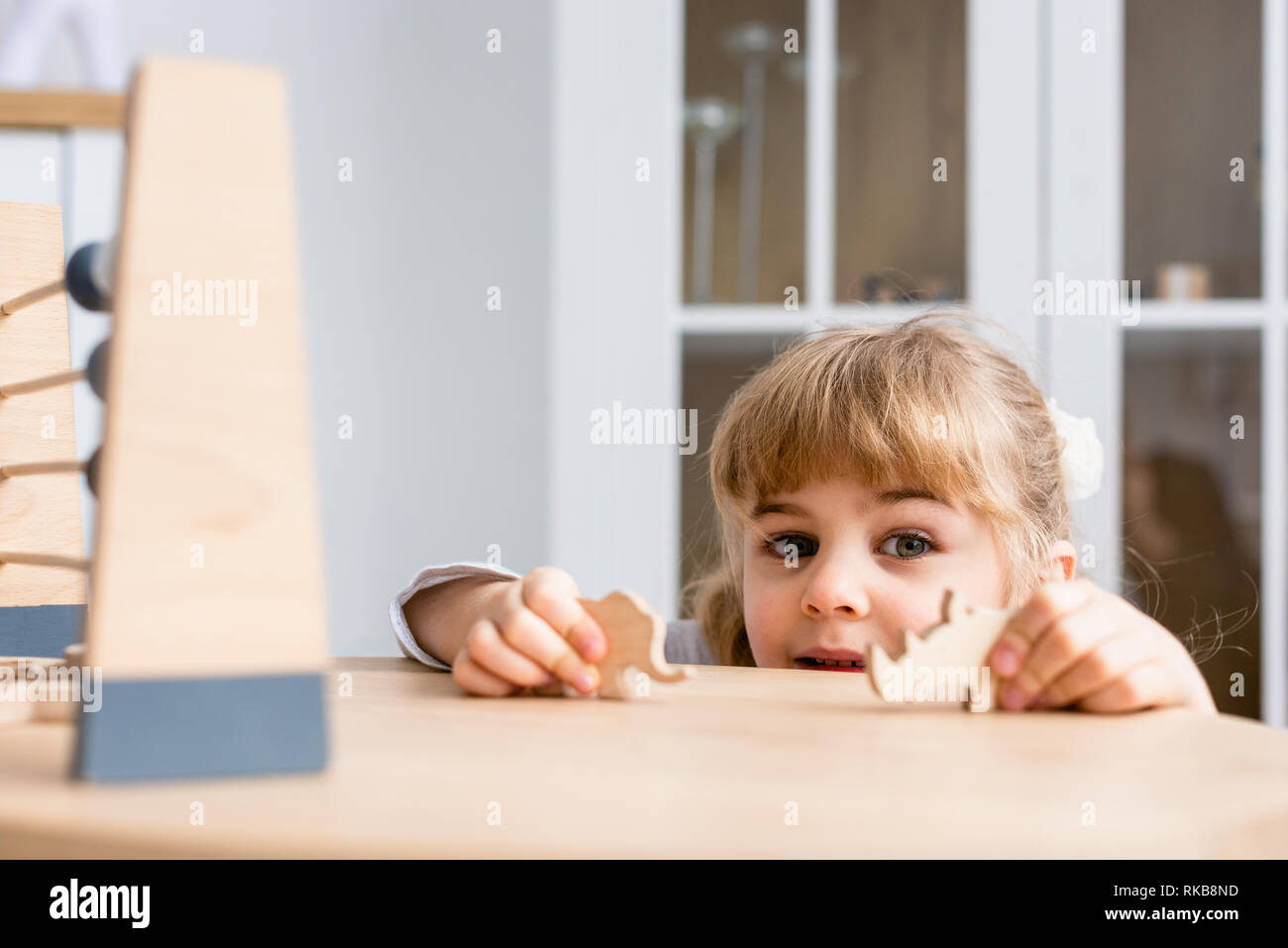 Small girl with wooden toys look out of table Stock Photo - Alamy