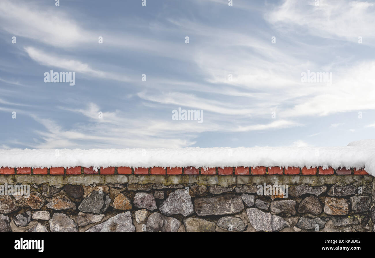 Stone wall covered by fresh snow in winter. A clear sky with soft white ...