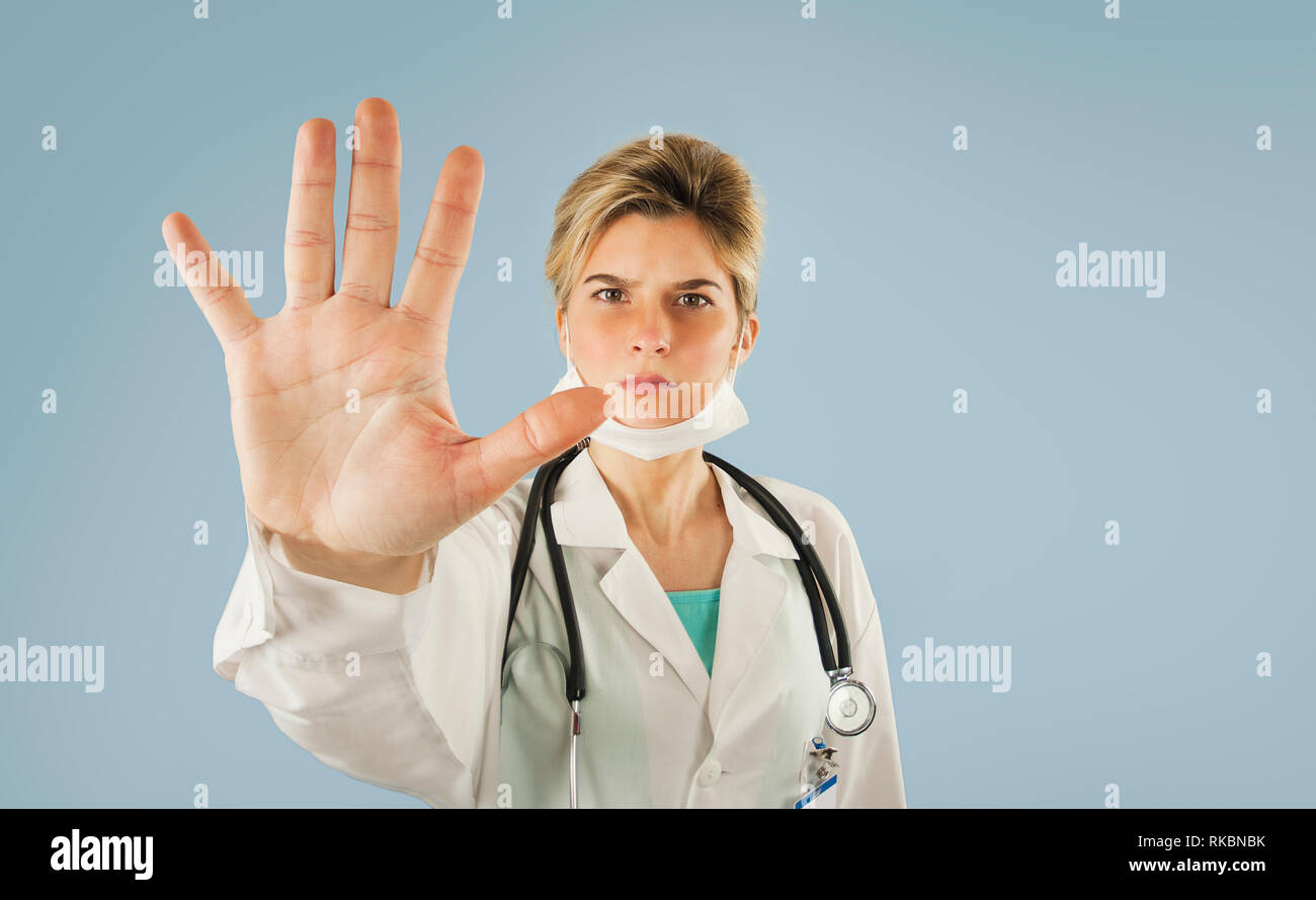Young girl doctor shows with hand palm stop sign on a blue isolated ...