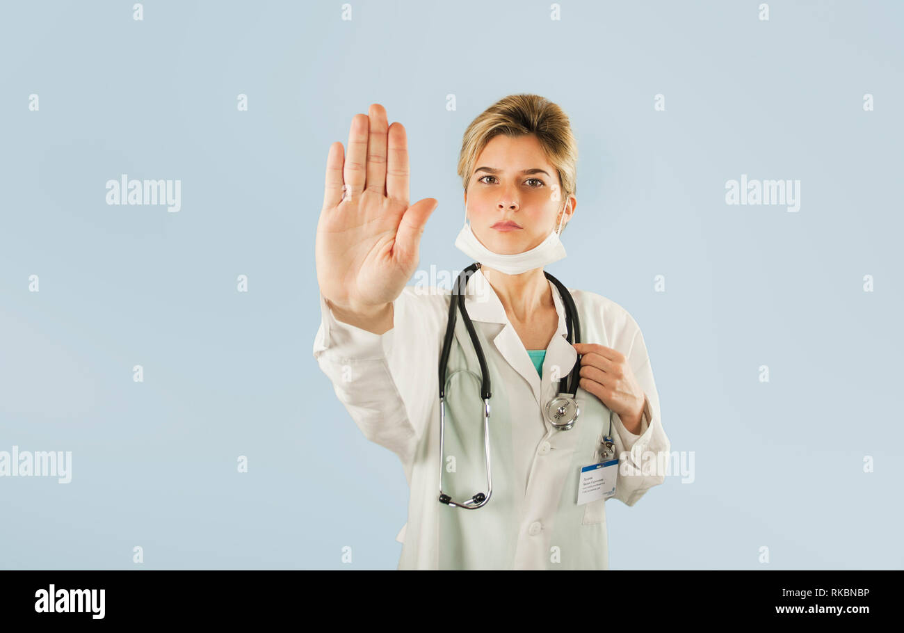 Young girl doctor shows with hand palm stop sign on a blue isolated ...