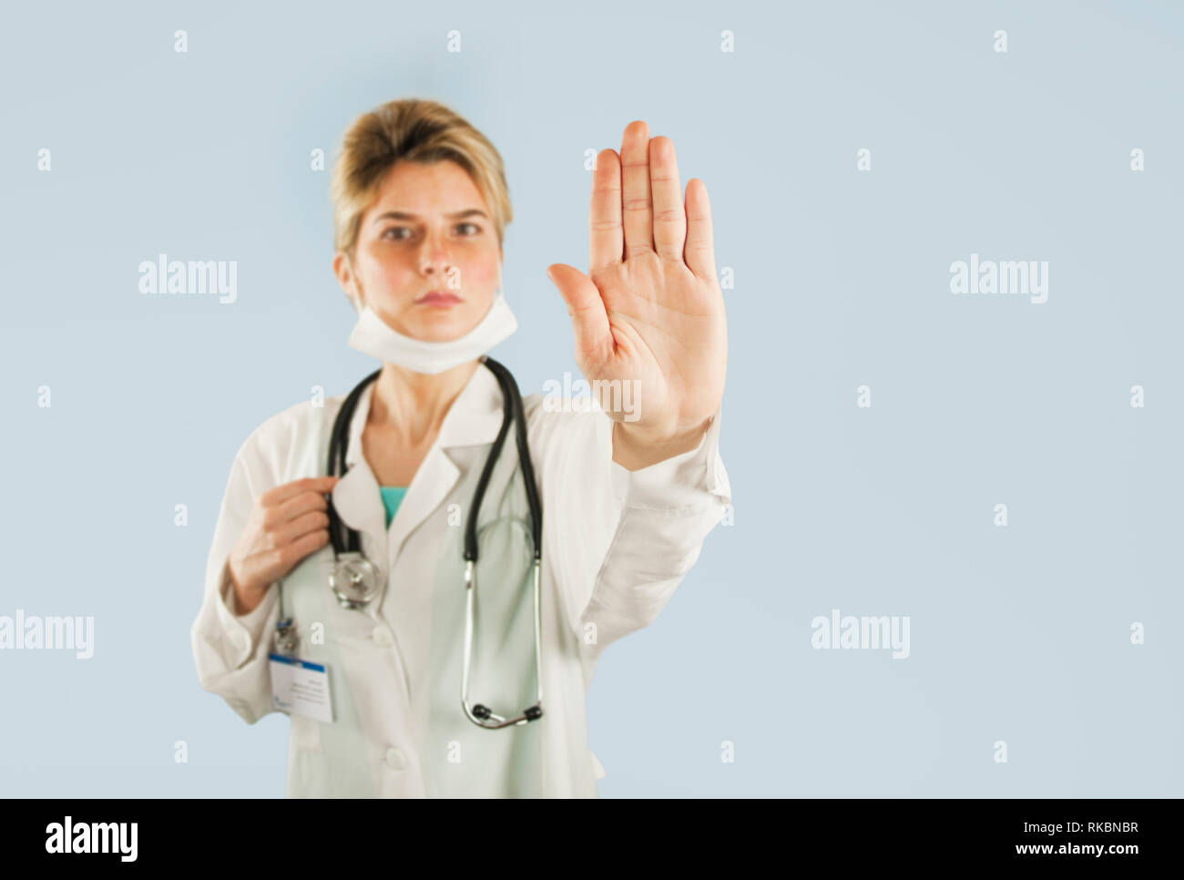 Young girl doctor shows with hand palm stop sign on a blue isolated ...