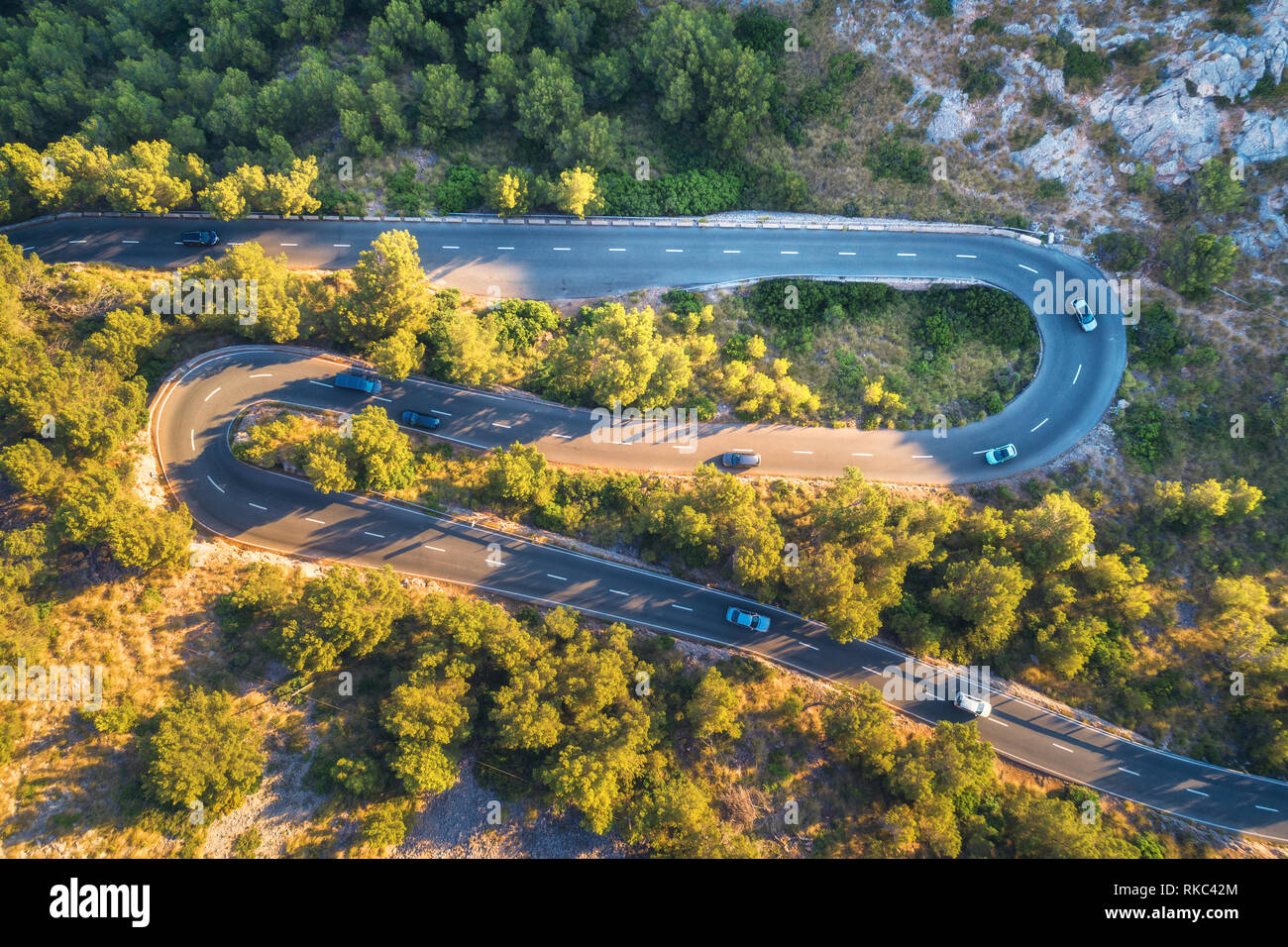 Aerial view of mountain curve road with cars, green forest at sunset in ...