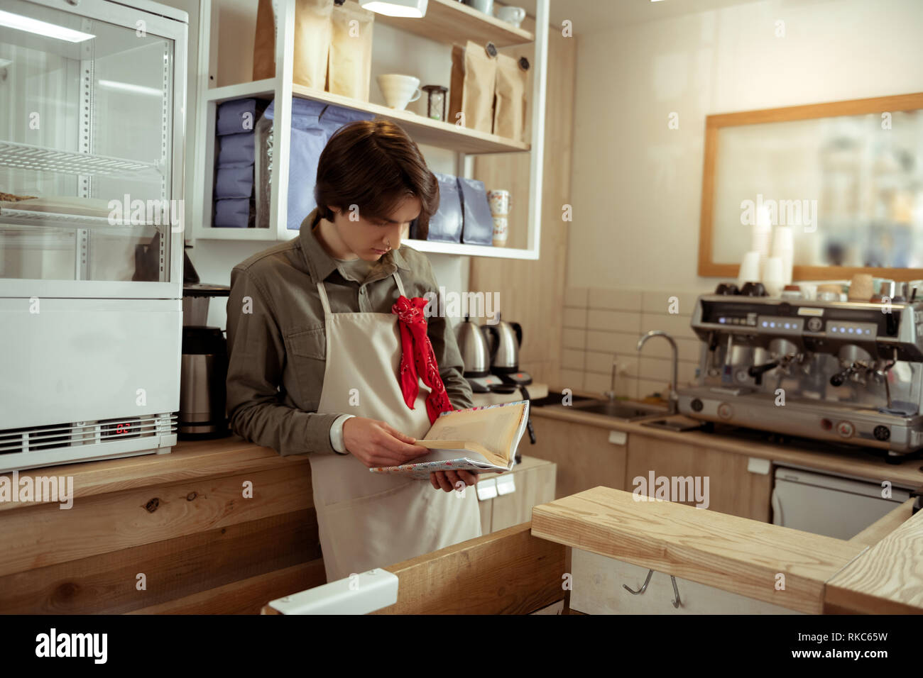 Focused curious barista wearing grey uniform and standing near desk ...