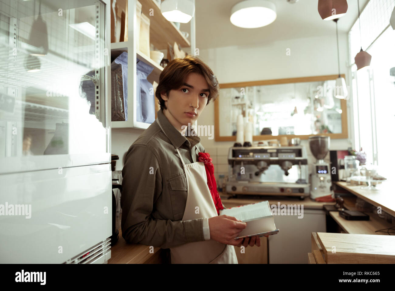 Dark-haired young barista with nose piercing flipping through book ...
