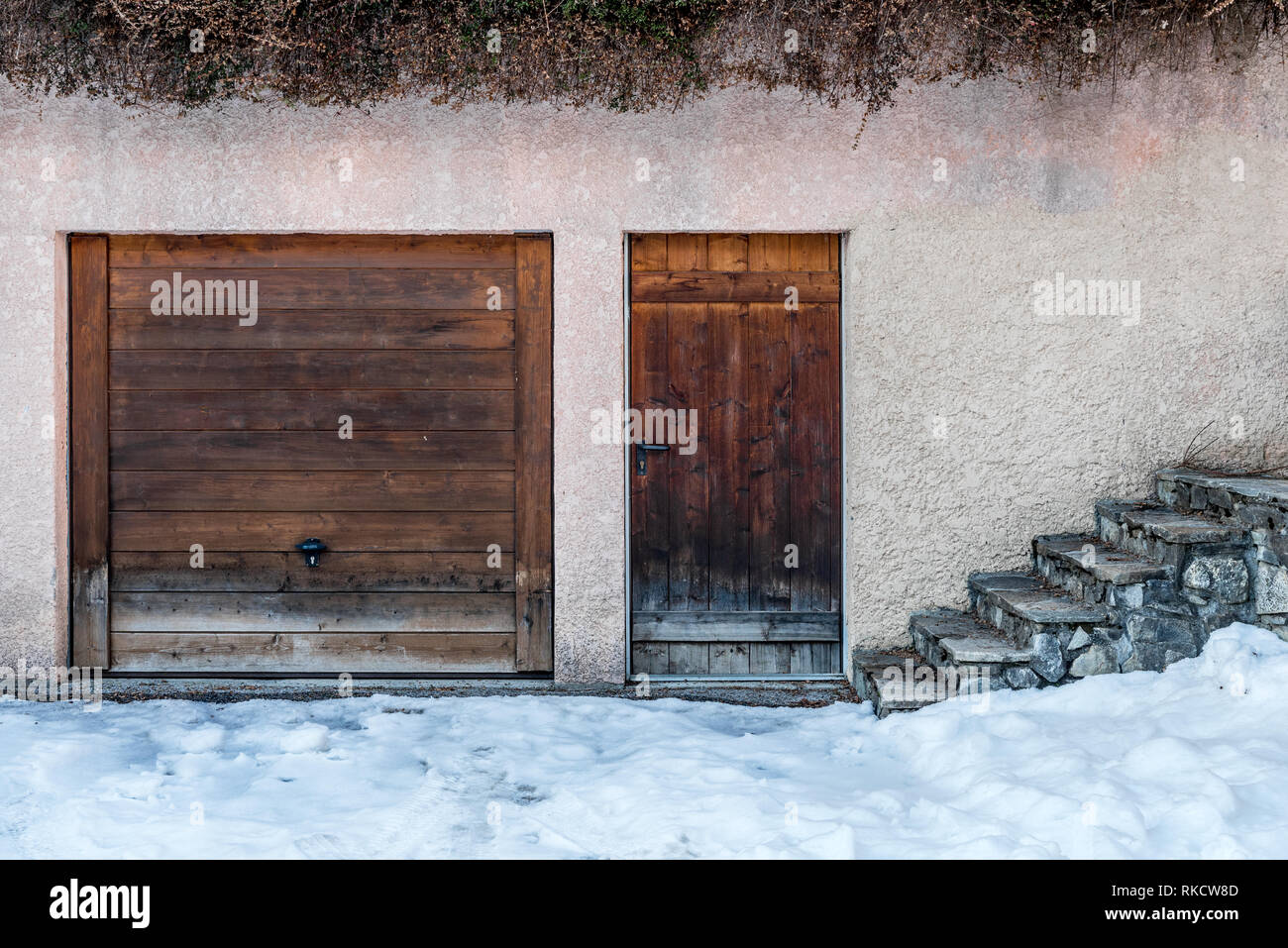 Wood garage and entry doors inset to rendered stone wall of outbuilding ...