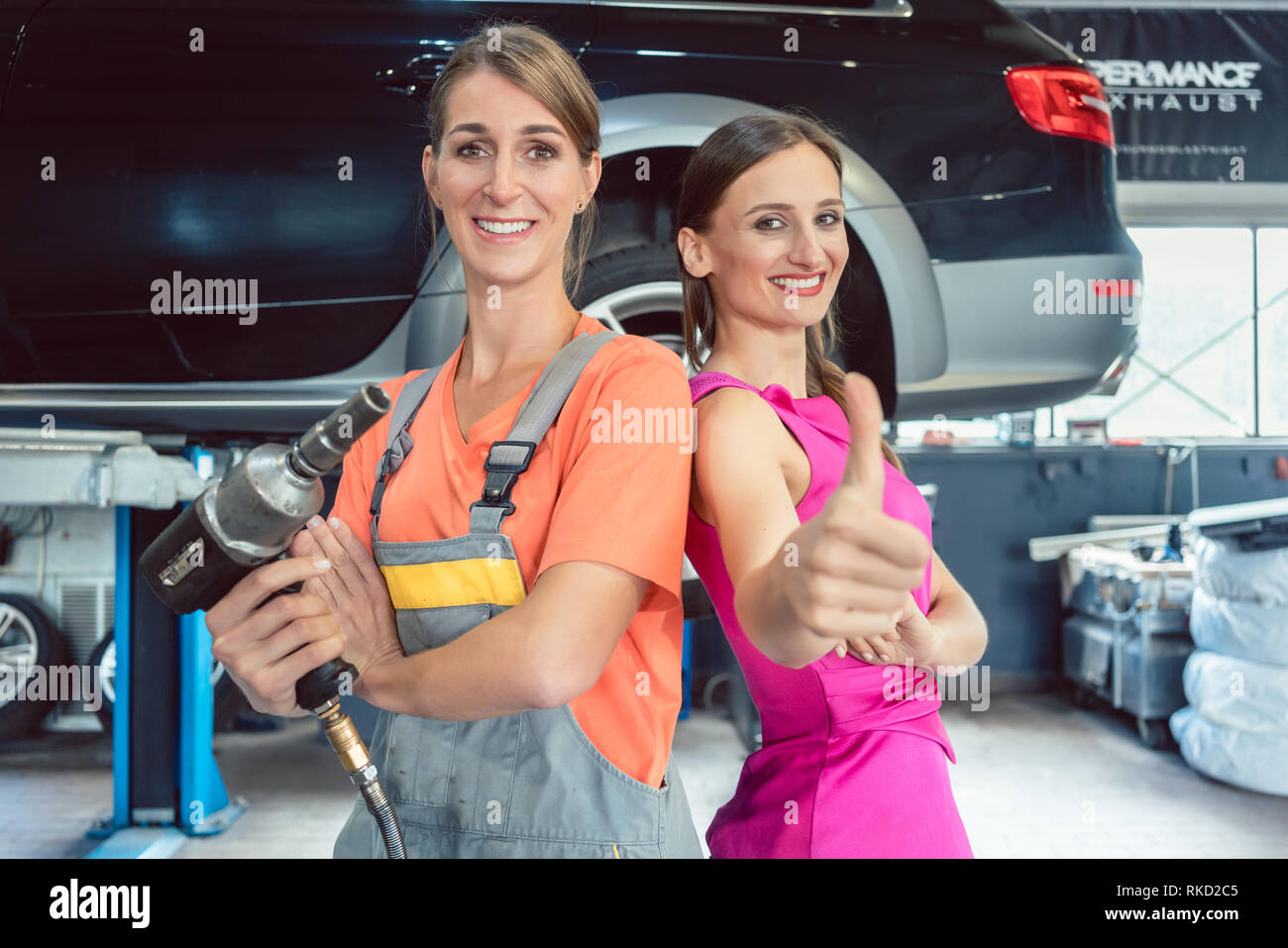 Portrait of a beautiful female auto mechanic next to her happy customer ...
