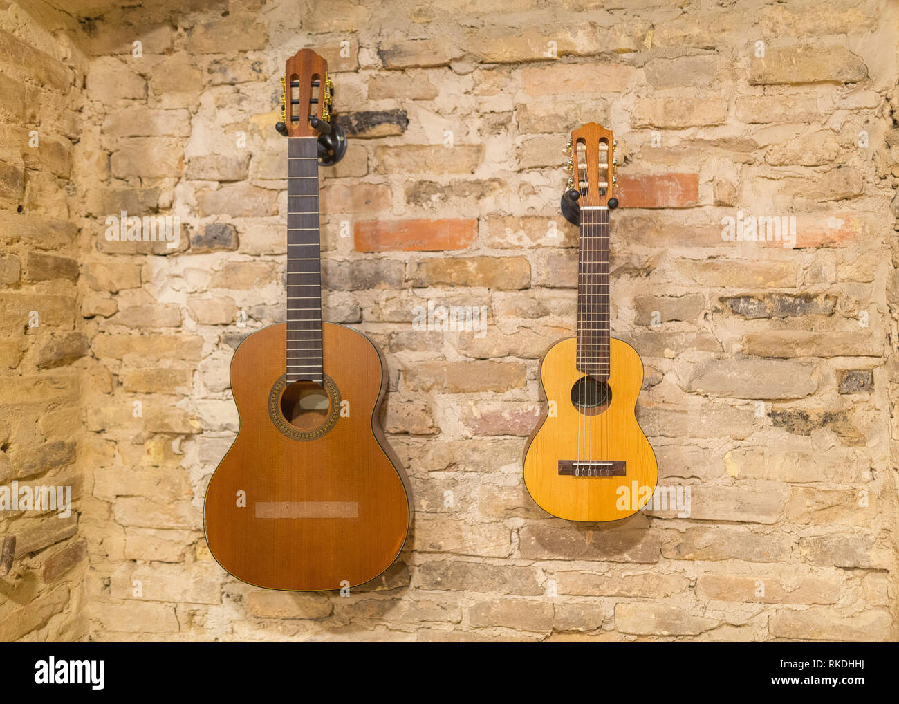 Two acoustic guitars hanging on brick wall background indoors. Vintage ...