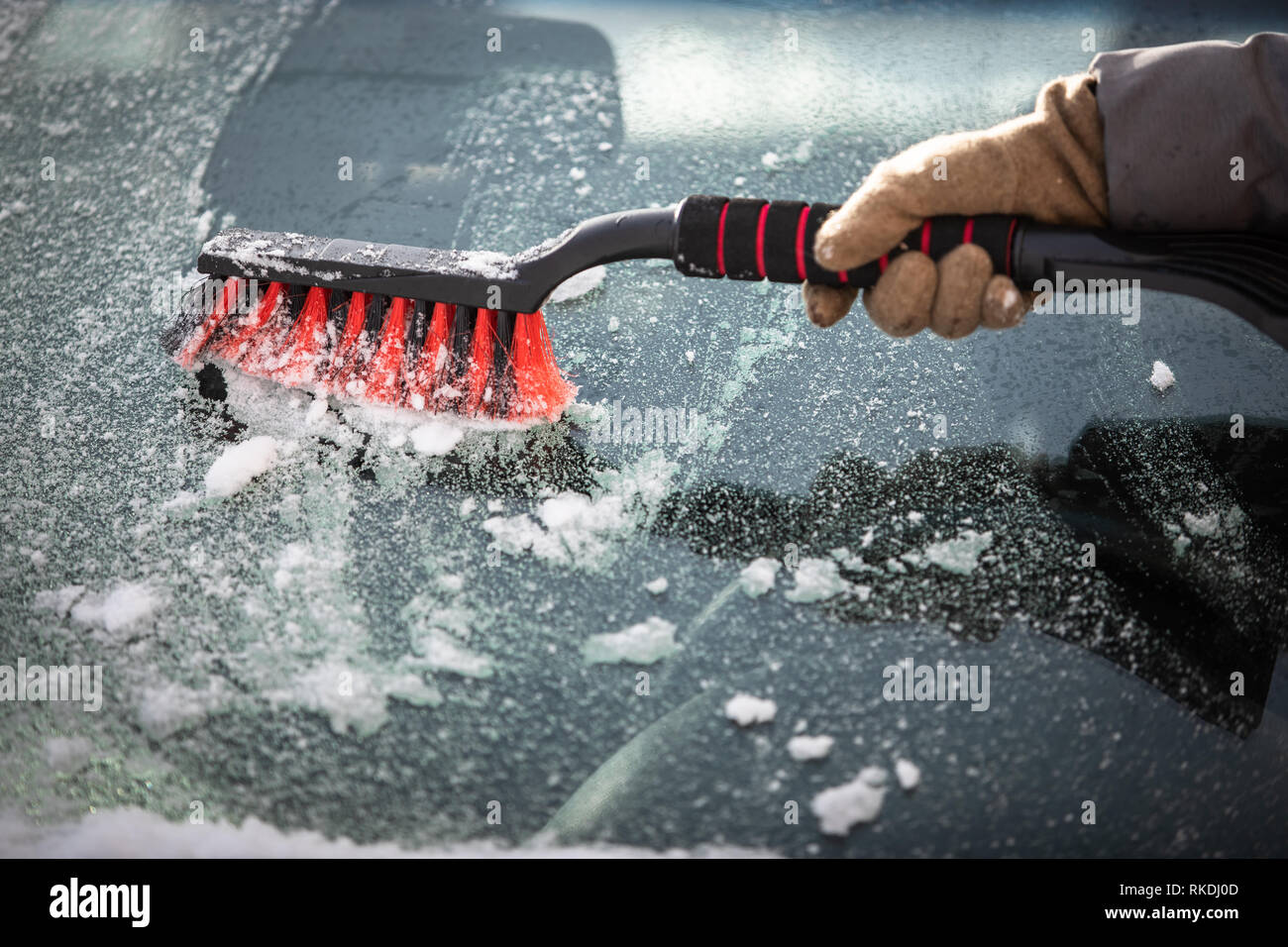 Pretty, young woman cleaning her car from snow after heavy snowstorm ...