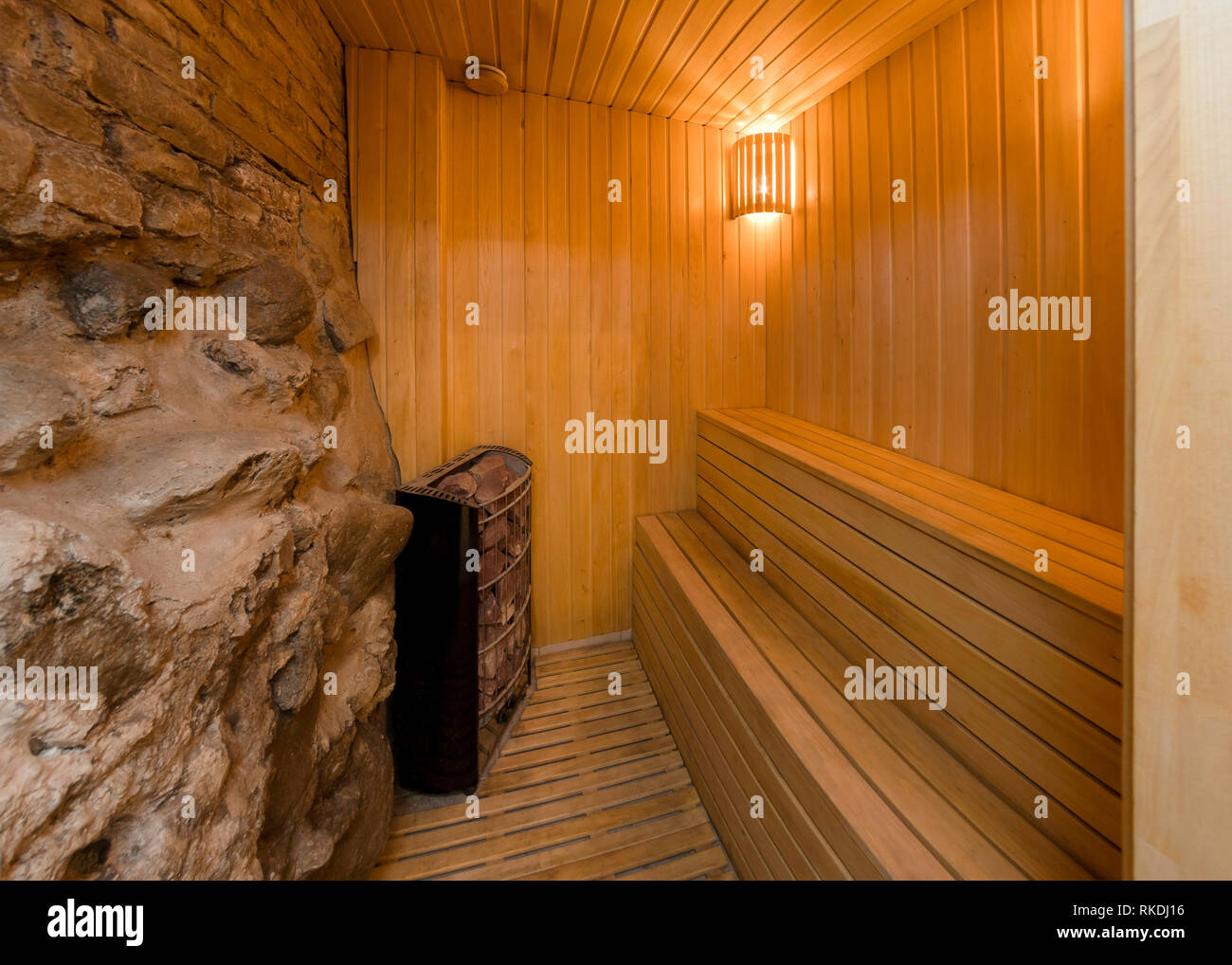 Inside of a modern day sauna, rock wall and wooden benches to sit on ...