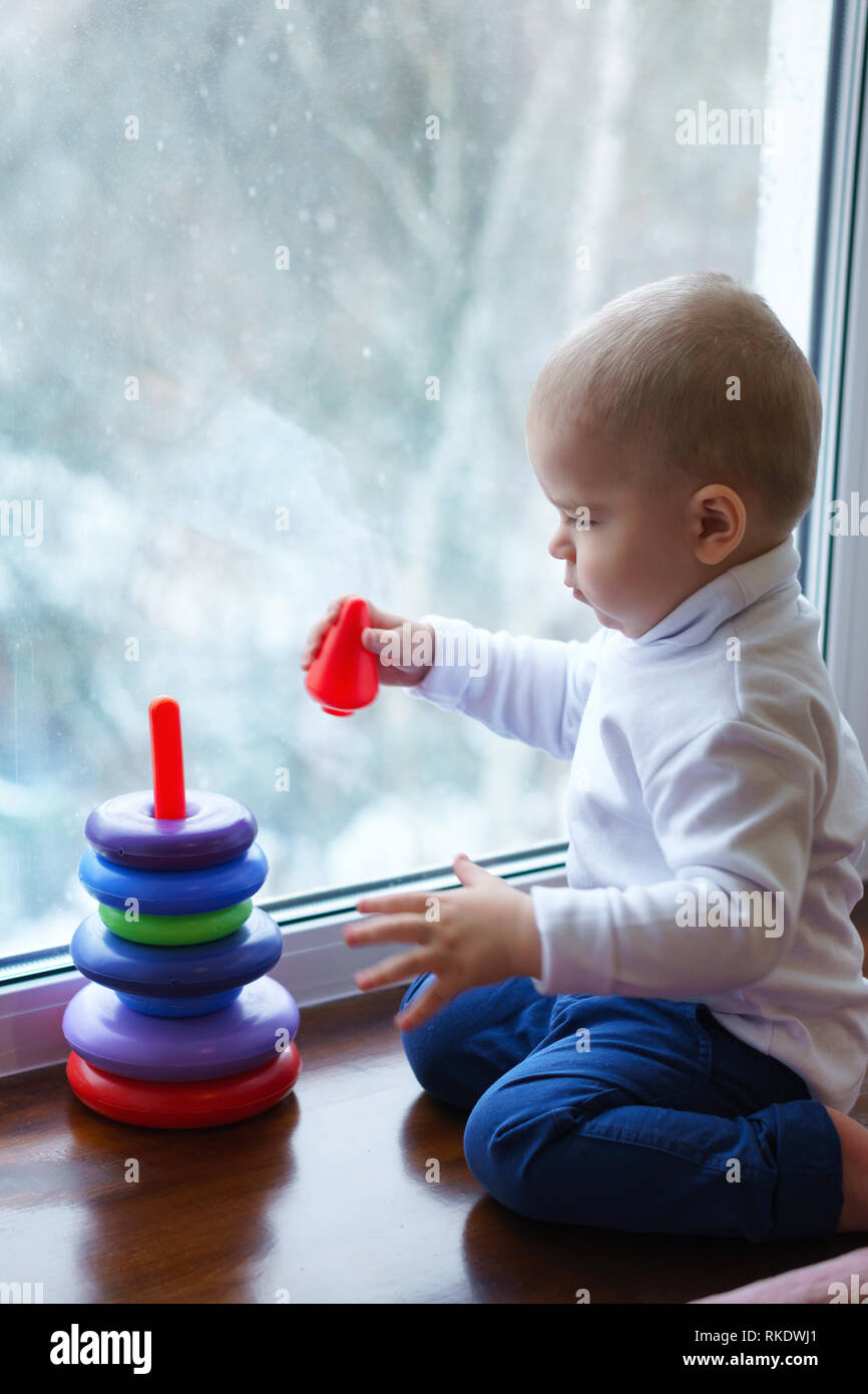 Little boy builds tower of multi-colored rings. Child is sitting on ...