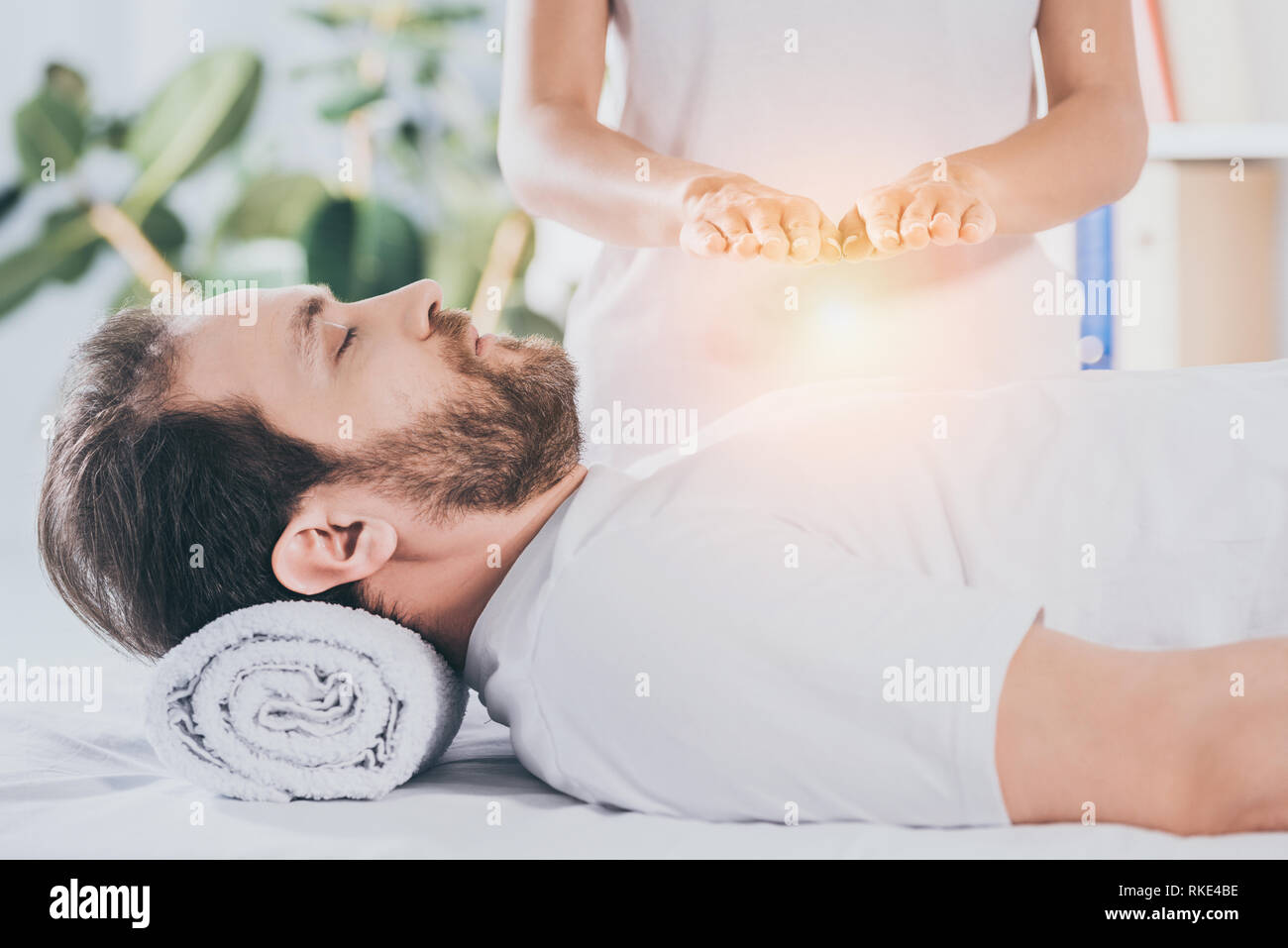 side view of calm bearded man with closed eyes receiving reiki ...