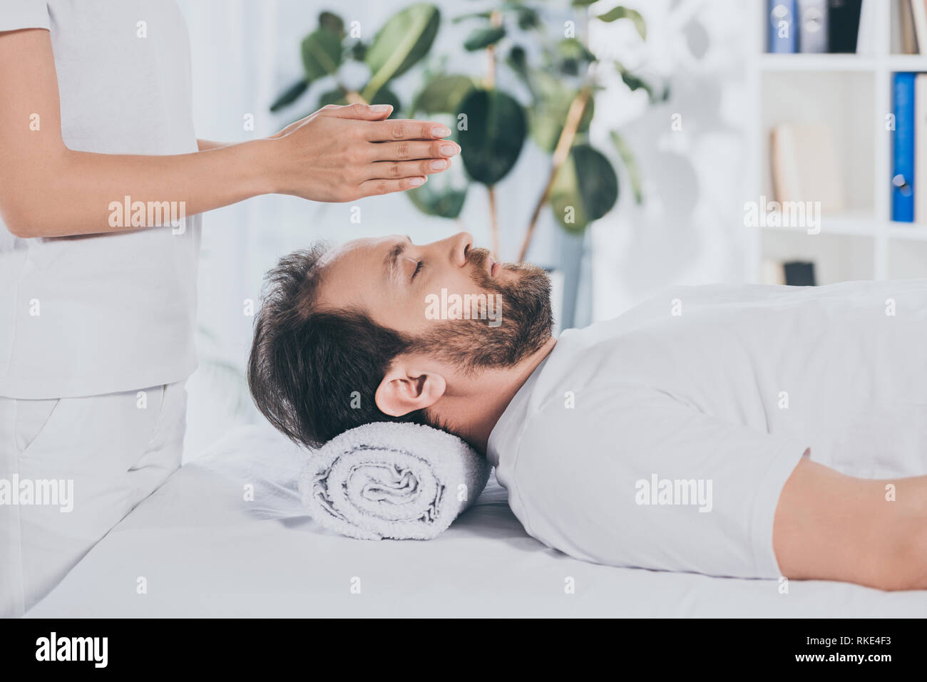 side view of bearded man with closed eyes receiving reiki treatment ...