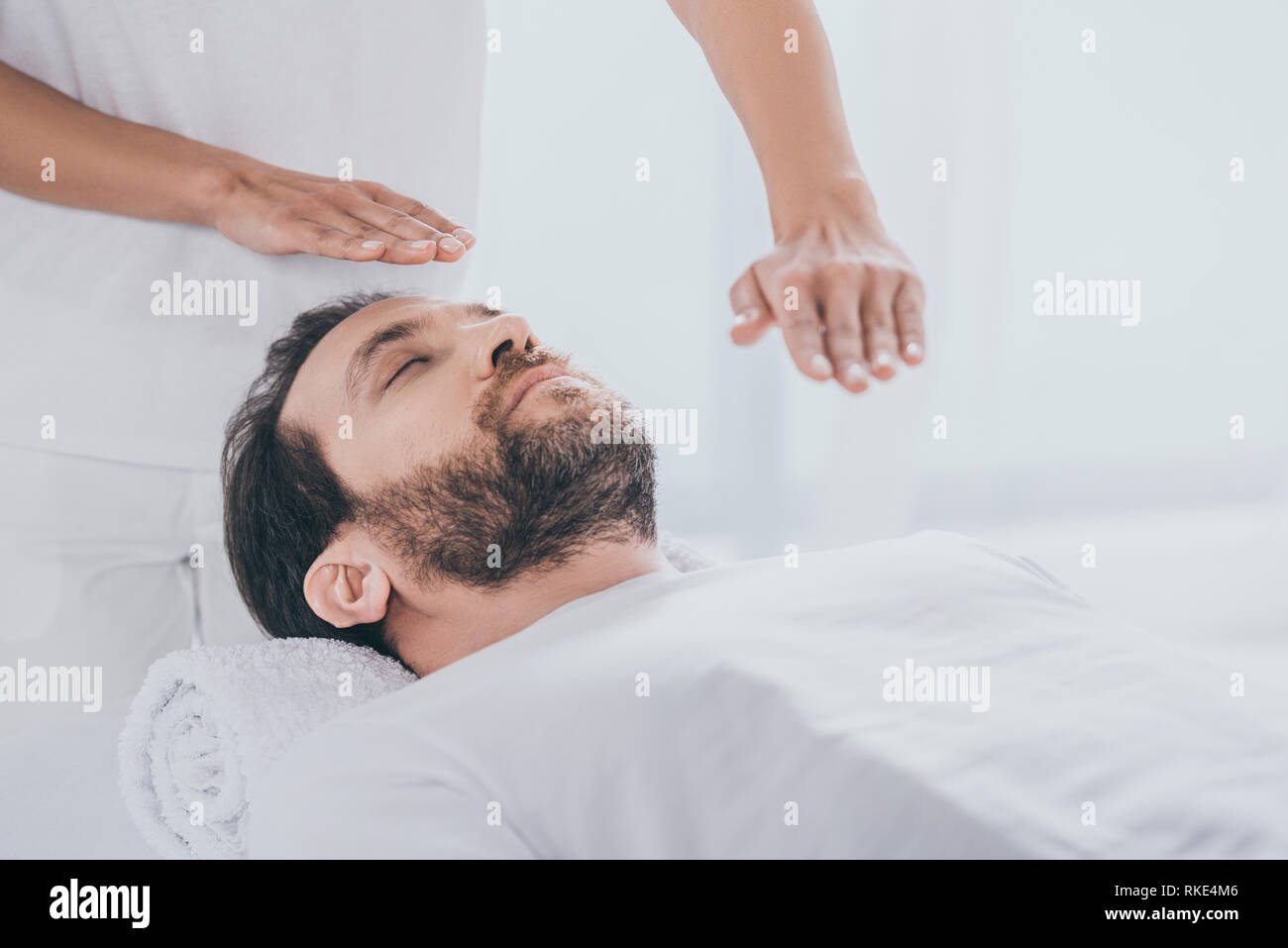Calm Bearded Man Lying On Massage Table And Hands Of Healer Doing Reiki Treatment Session Stock