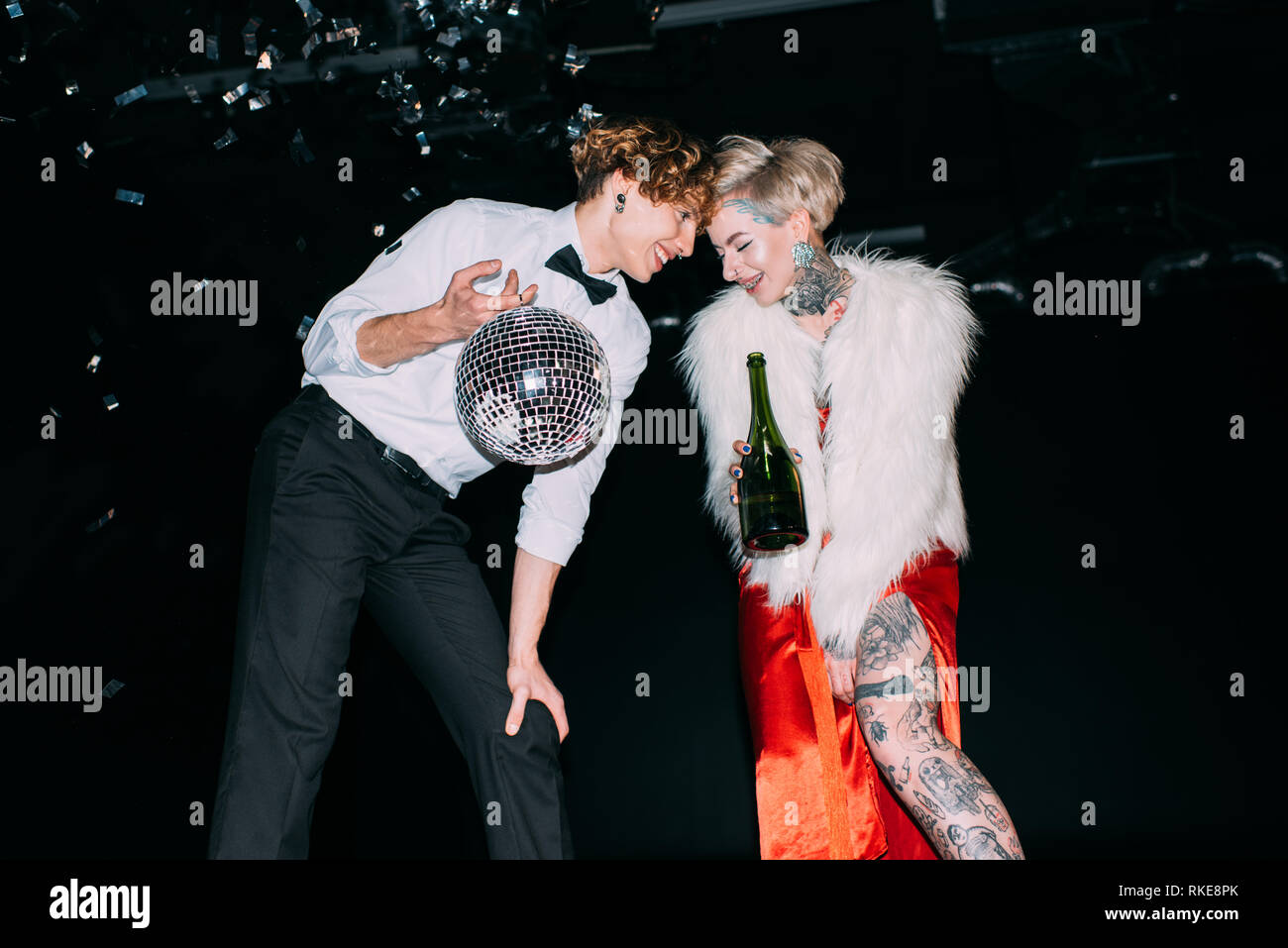 man holding disco ball and standing near woman with bottle of alcohol ...