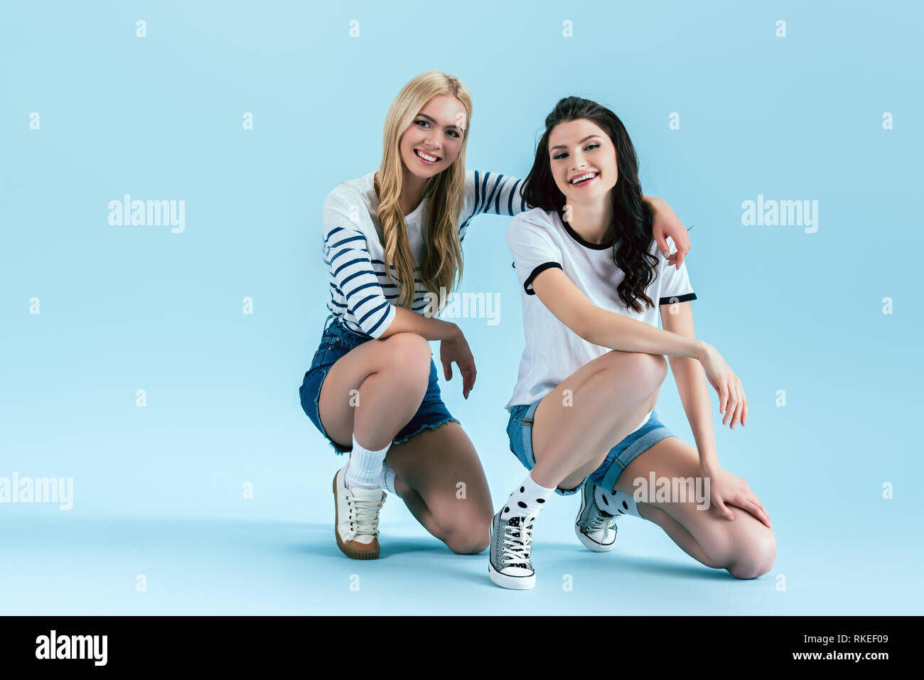 Cute girls squatting and embracing on blue background Stock Photo - Alamy