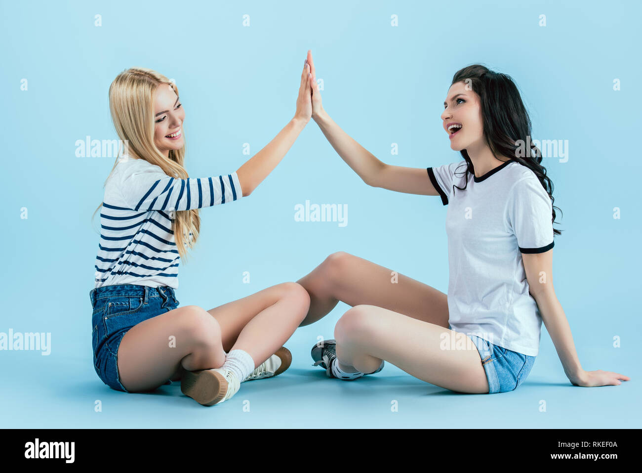 Cheerful girls in denim shorts posing on floor on blue background Stock ...