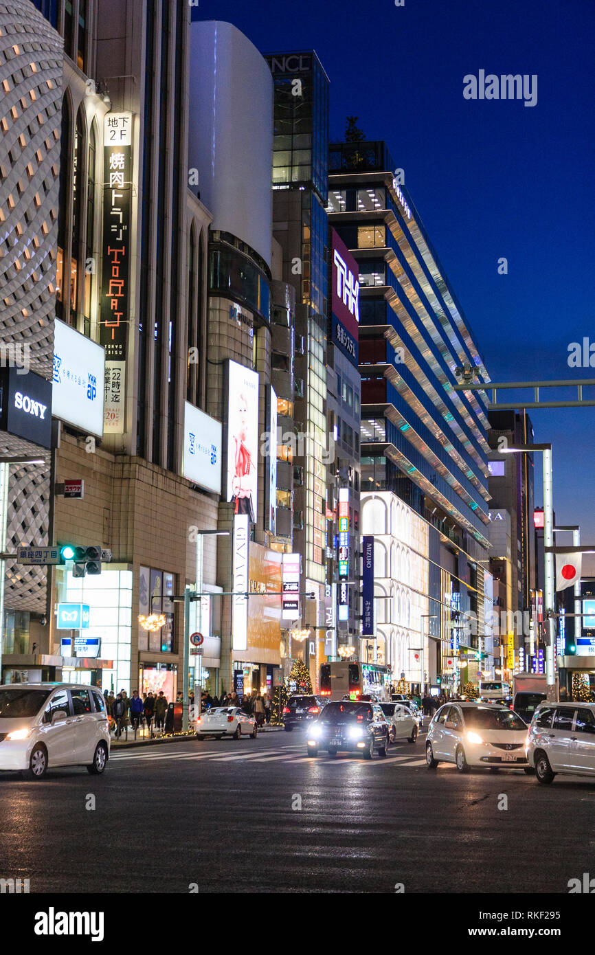 Tokyo, Ginza, night. Traffic turning at the 4-chome junction with view along buildings and the ...