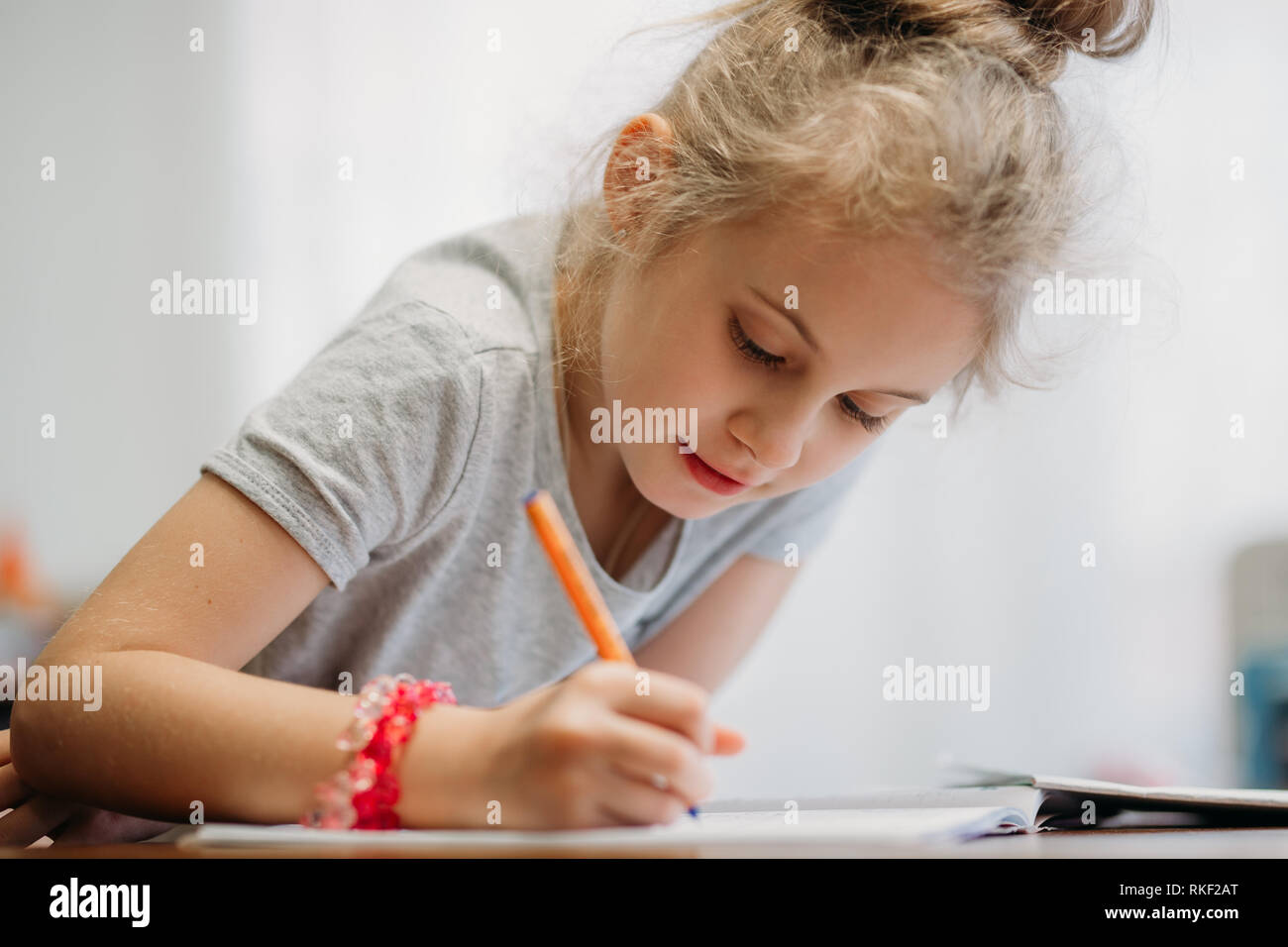 A seven-year-old girl sits at home at a table and writes in a notebook ...