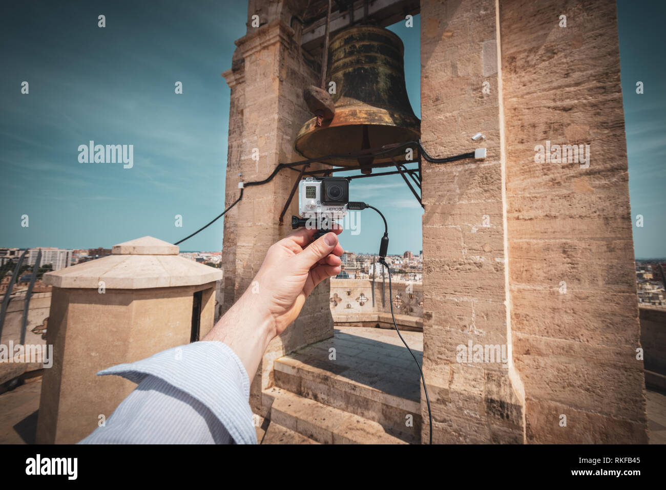 A man holds a GoPro camera in front of a large bell at the top of the ...