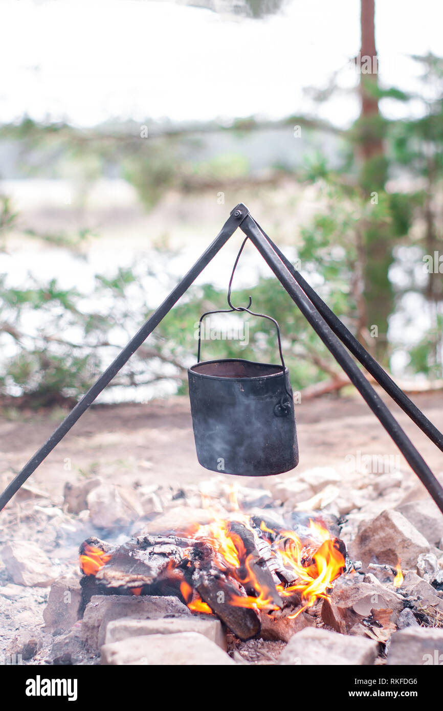 Tourist pot hanging over burning fire on tripod. Cooking in camping ...
