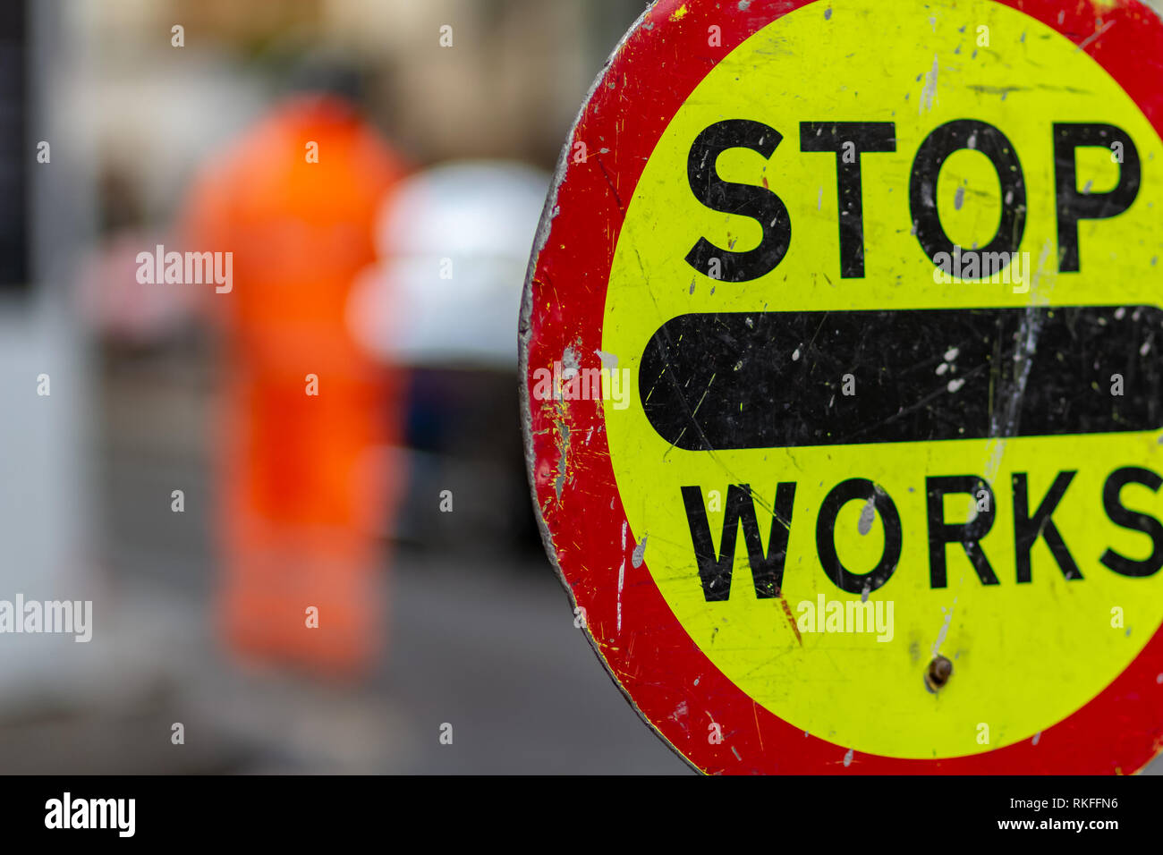 Warning sign Stop Works and a man in orange working in background on ...