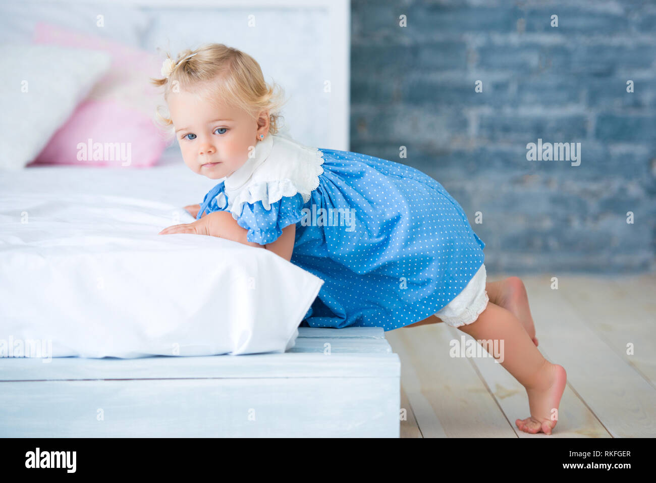 Cute little girl in blue dress lying on the bed in the interior ...