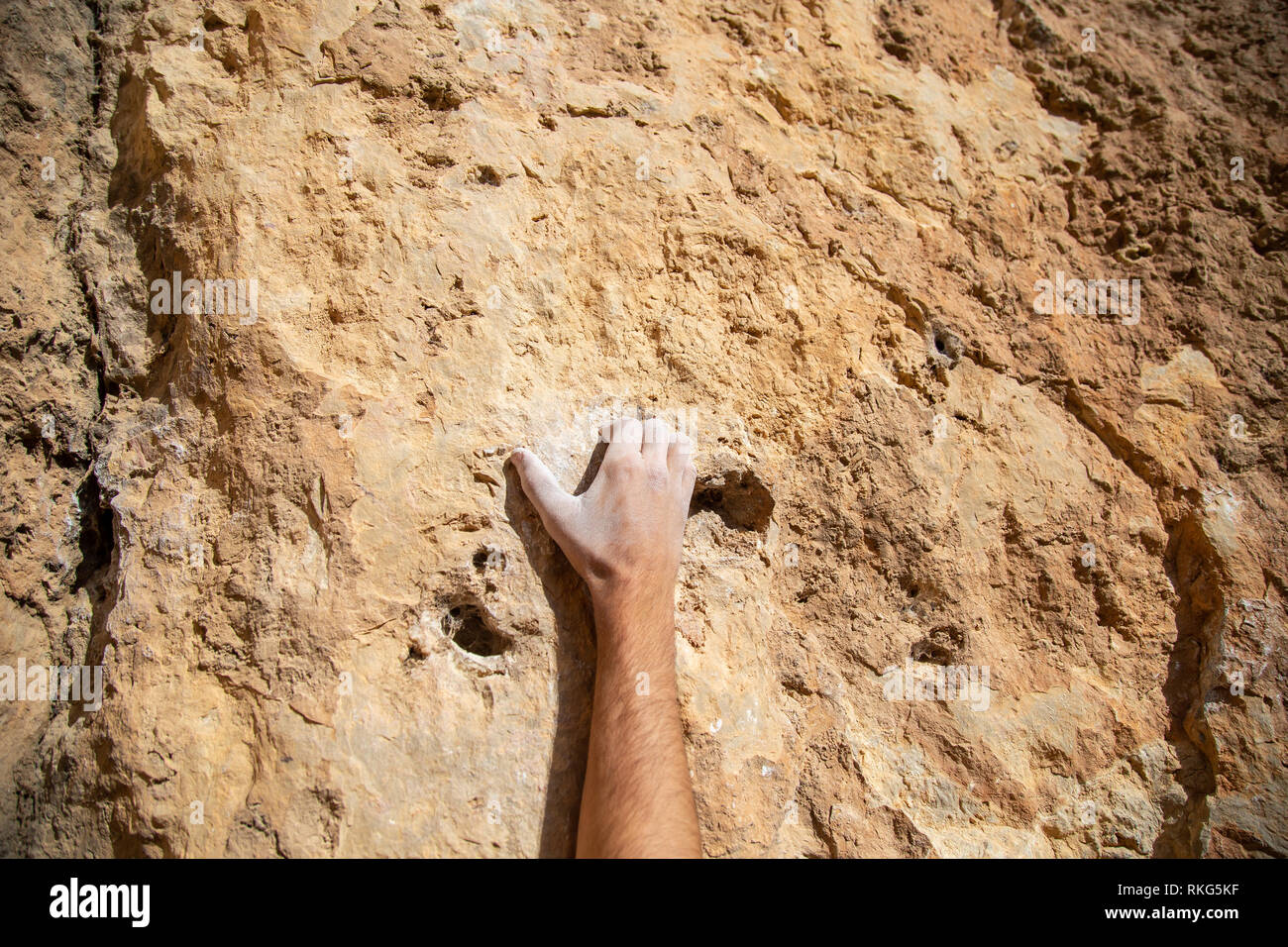 Crop male hand in white chalk powder hanging on rough rock while ...