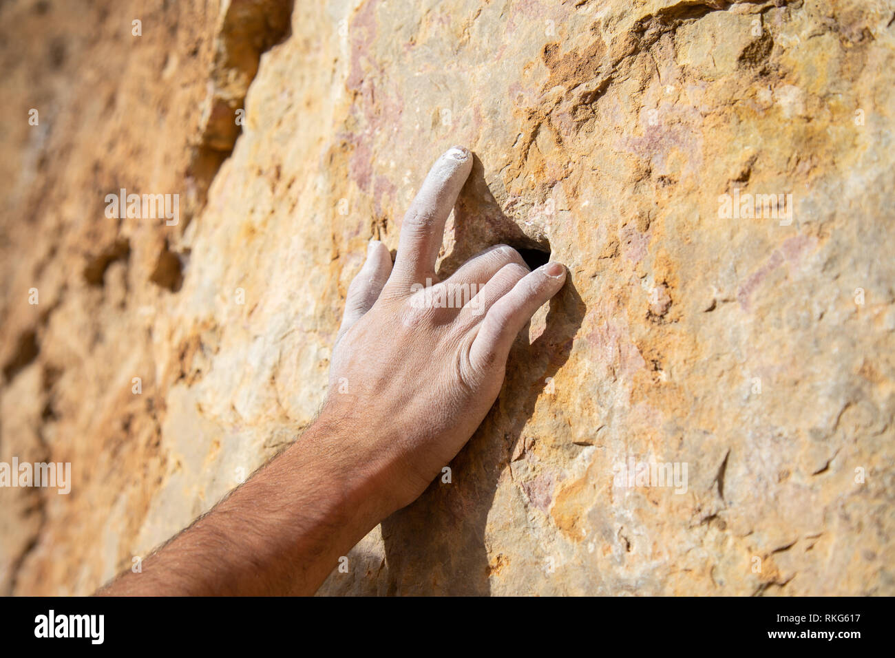 Crop male hand in white chalk powder hanging on rough rock while ...