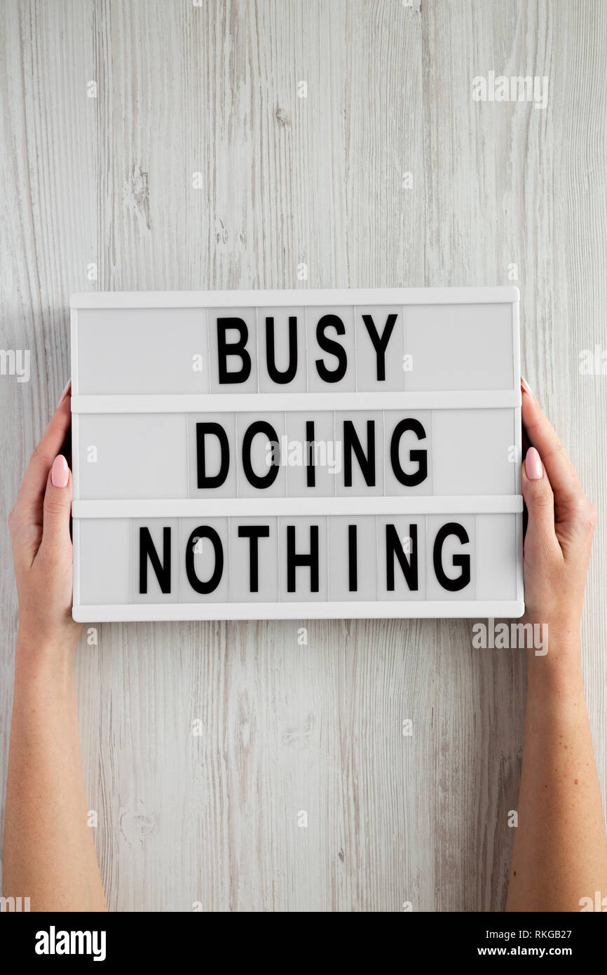 Female hands hold lightbox with text 'Busy doing nothing' on a white ...