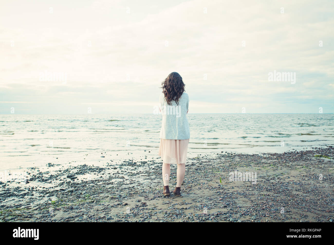 Beautiful girl standing alone on the coastline of the sea and looking ...
