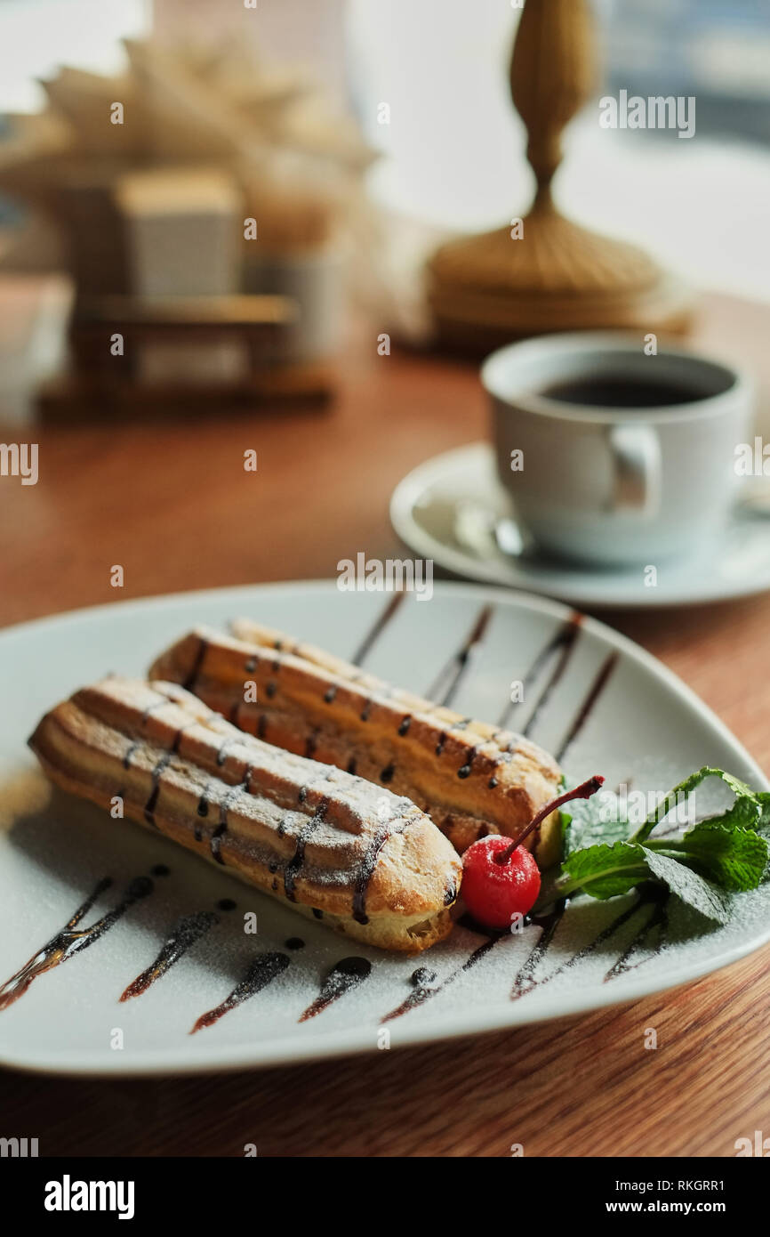 Two sweet french eclairs on plate. Breakfast in cafe. wooden table ...