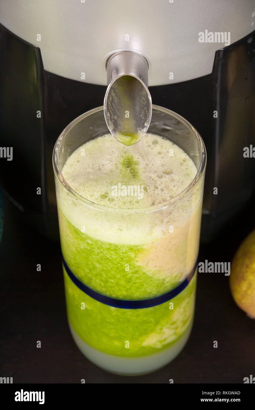 A juicer pouring fruit and vegetable juice into a drinking glass on a ...