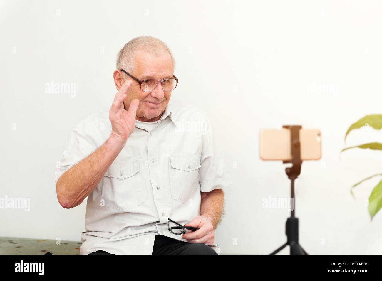 Smiling eldery man looking at camera making video blog or call at home ...