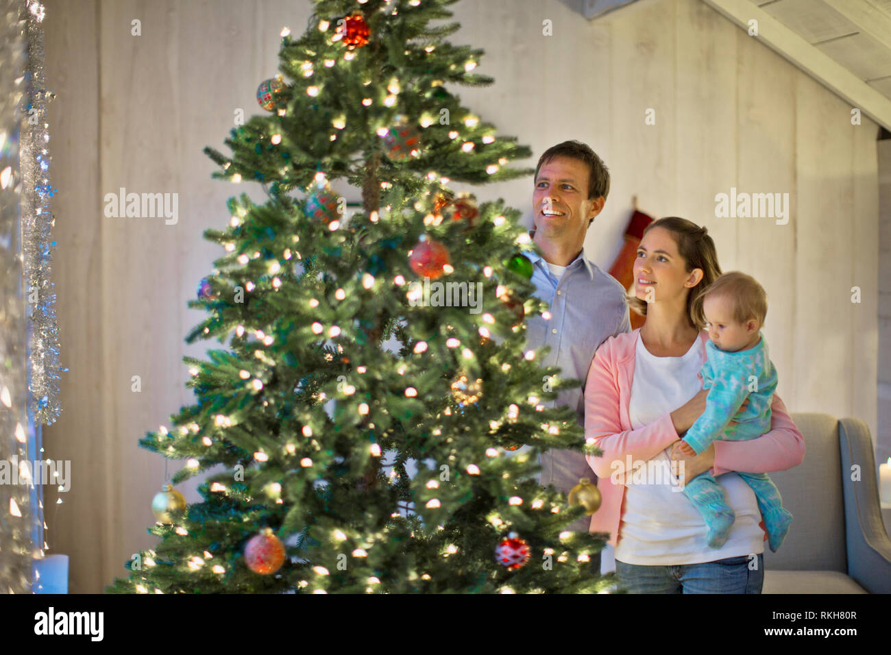 Couple and their baby admiring the Christmas tree Stock Photo - Alamy