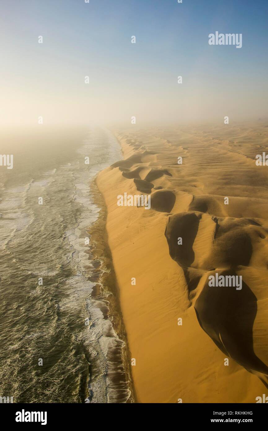 Aerial view of coastline with sandunes of the Namib desert floating in ...