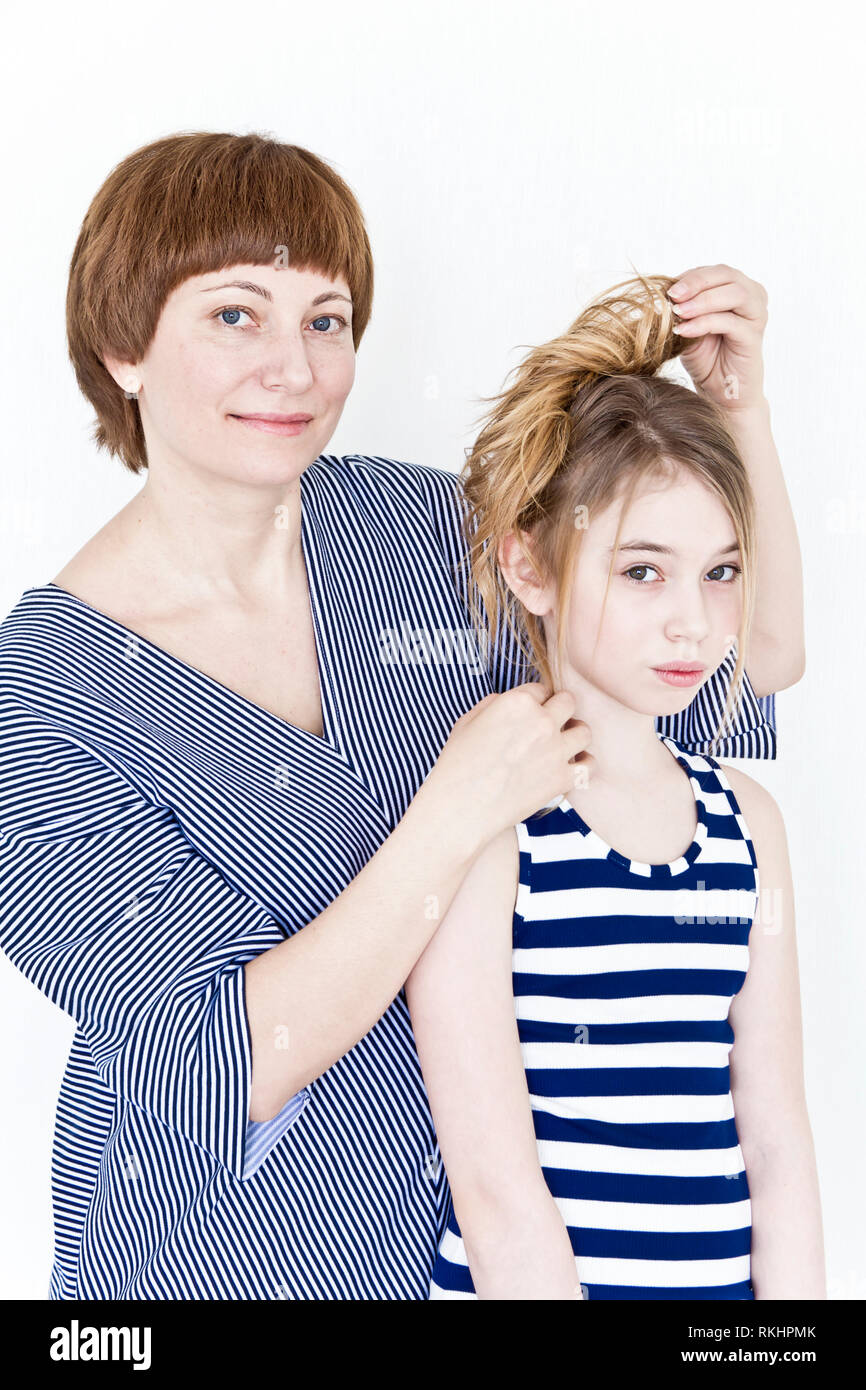 Mother is making hairstyle to her daughter near white wall in striped ...