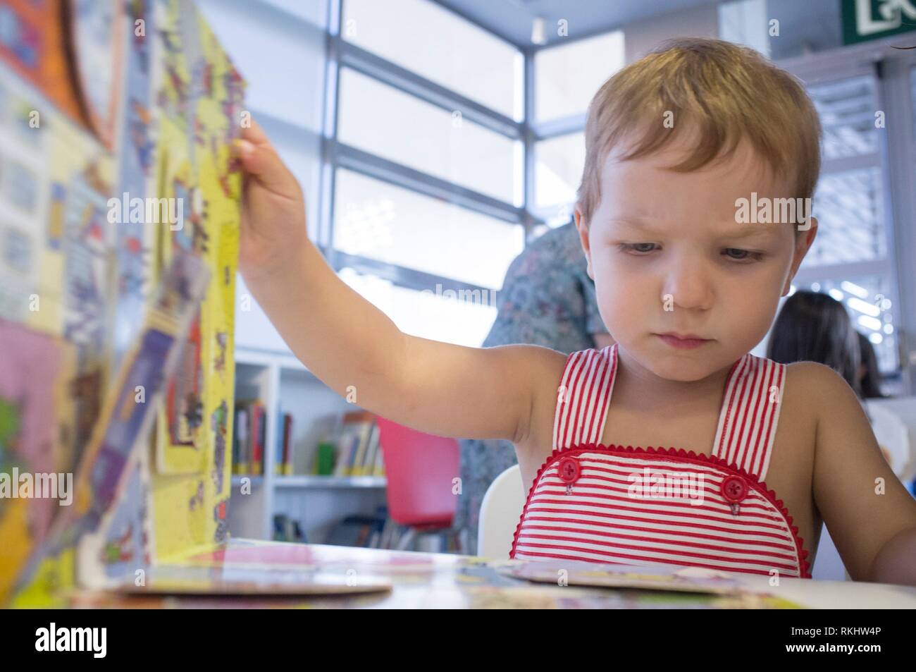 Cute 2 years boy turning a pop-up book page at library. Discovering the ...