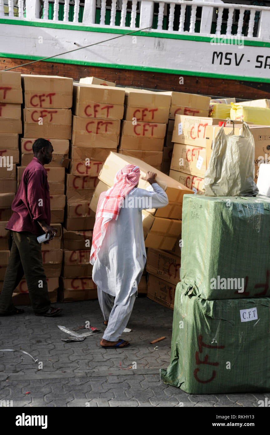 A dock worker stacking large cartons to be loaded onto a moored Dhow ...