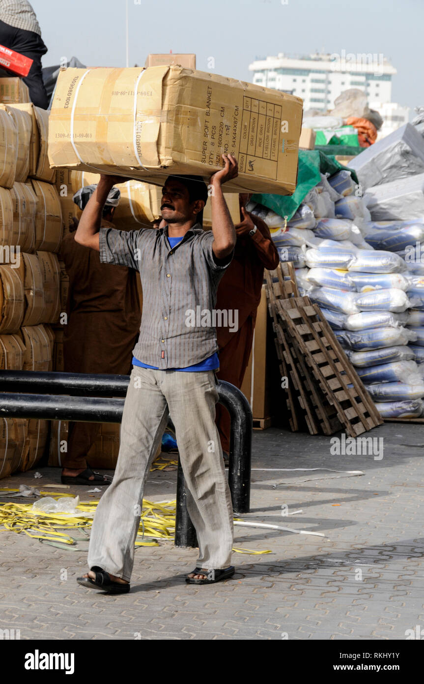 An Asian dock worker carrying a large heavy cartons to be loaded onto a ...