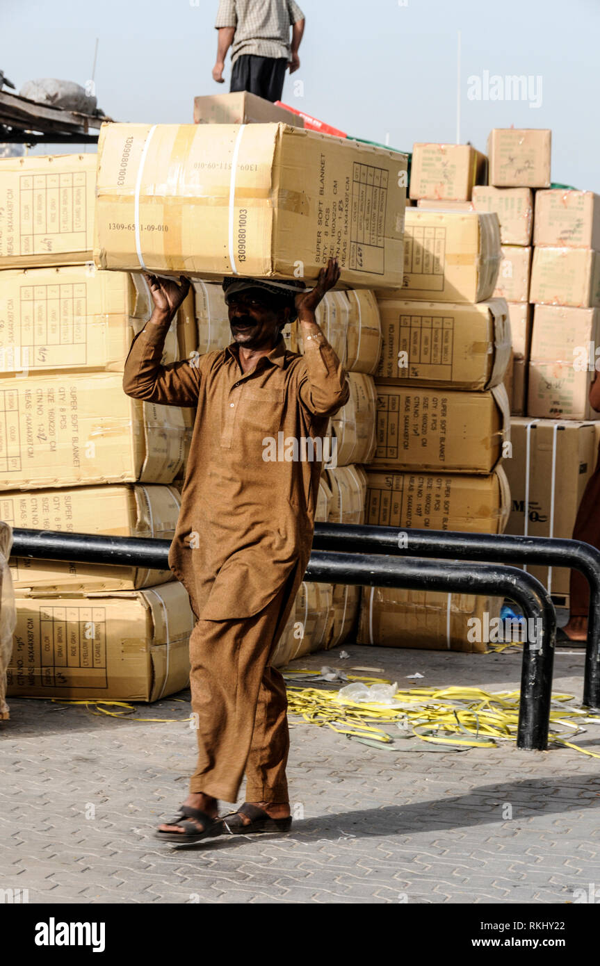 An Asian dock worker carrying a large heavy cartons to be loaded onto a ...