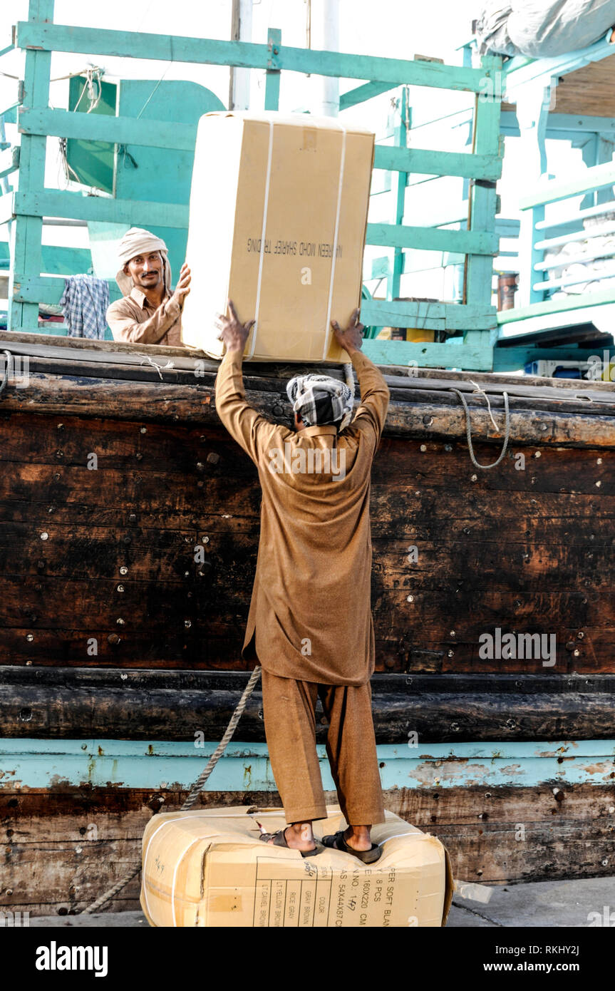 An Asian dock worker carrying a large heavy cartons to a boat crew ...