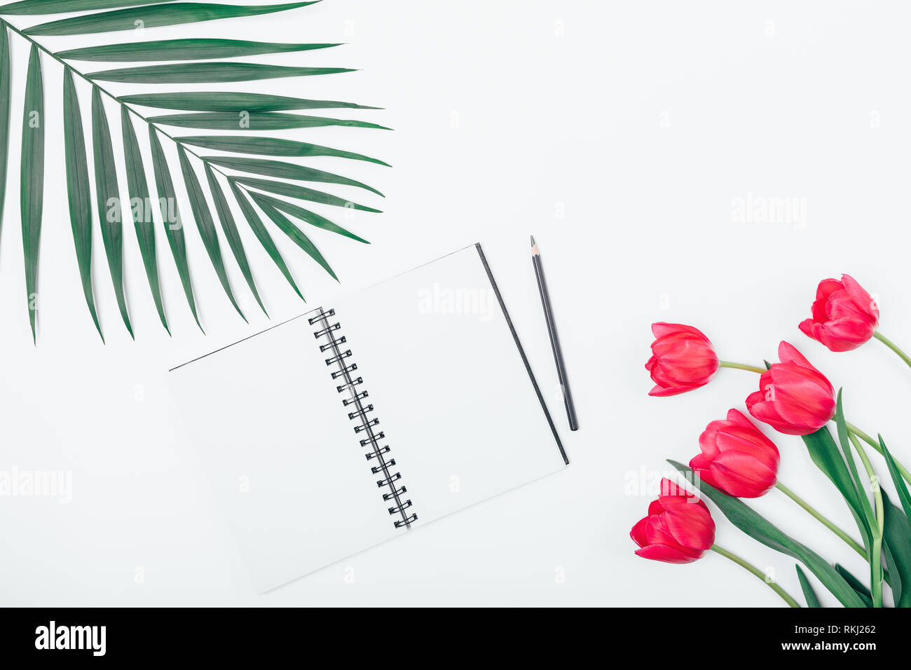 Flat lay floral arrangement of open blank notebook with pencil next to ...